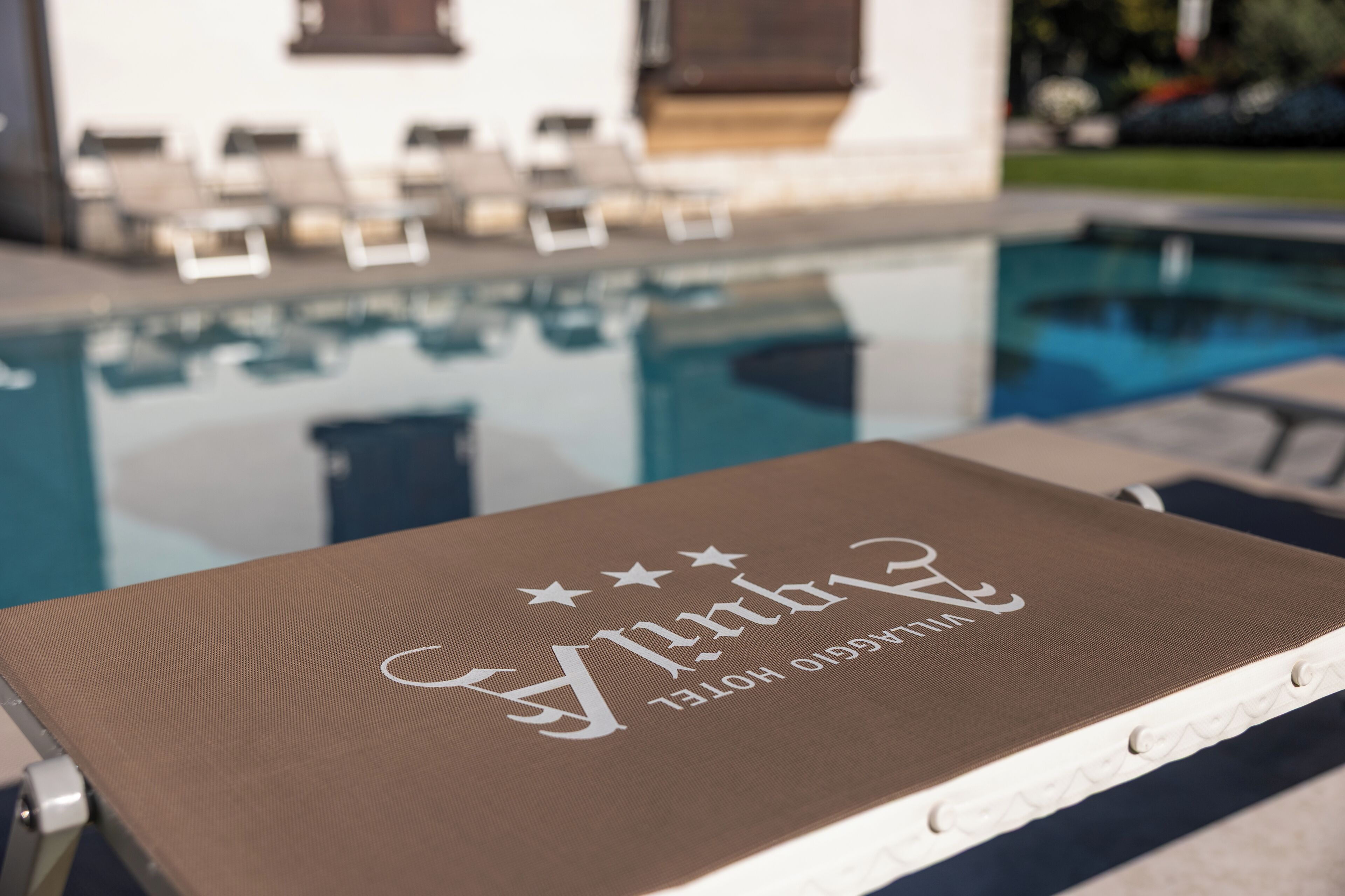 Uma espreguiçadeira junto à piscina, com capa exibindo o nome e o logotipo do hotel.