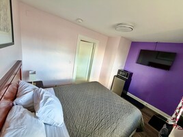 Um quarto com cama, televisão na parede e micro-ondas sobre uma mesinha.