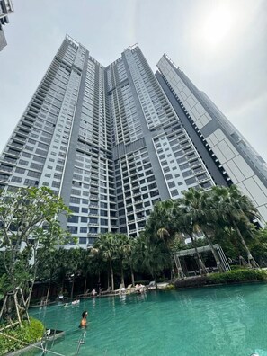 Um edifício alto com vários andares, piscina e palmeiras.