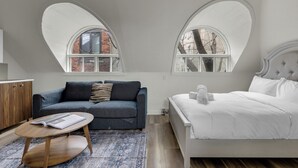 Quarto com cama, sofá, mesa de centro e duas janelas em arco.