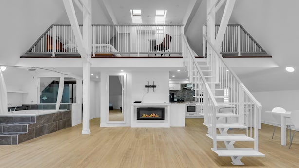 Um amplo loft com pé direito alto, lareira, escada e área de jantar.
