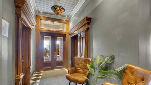 Um hall com piso xadrez, uma poltrona de couro com capitonê e um vaso de plantas.