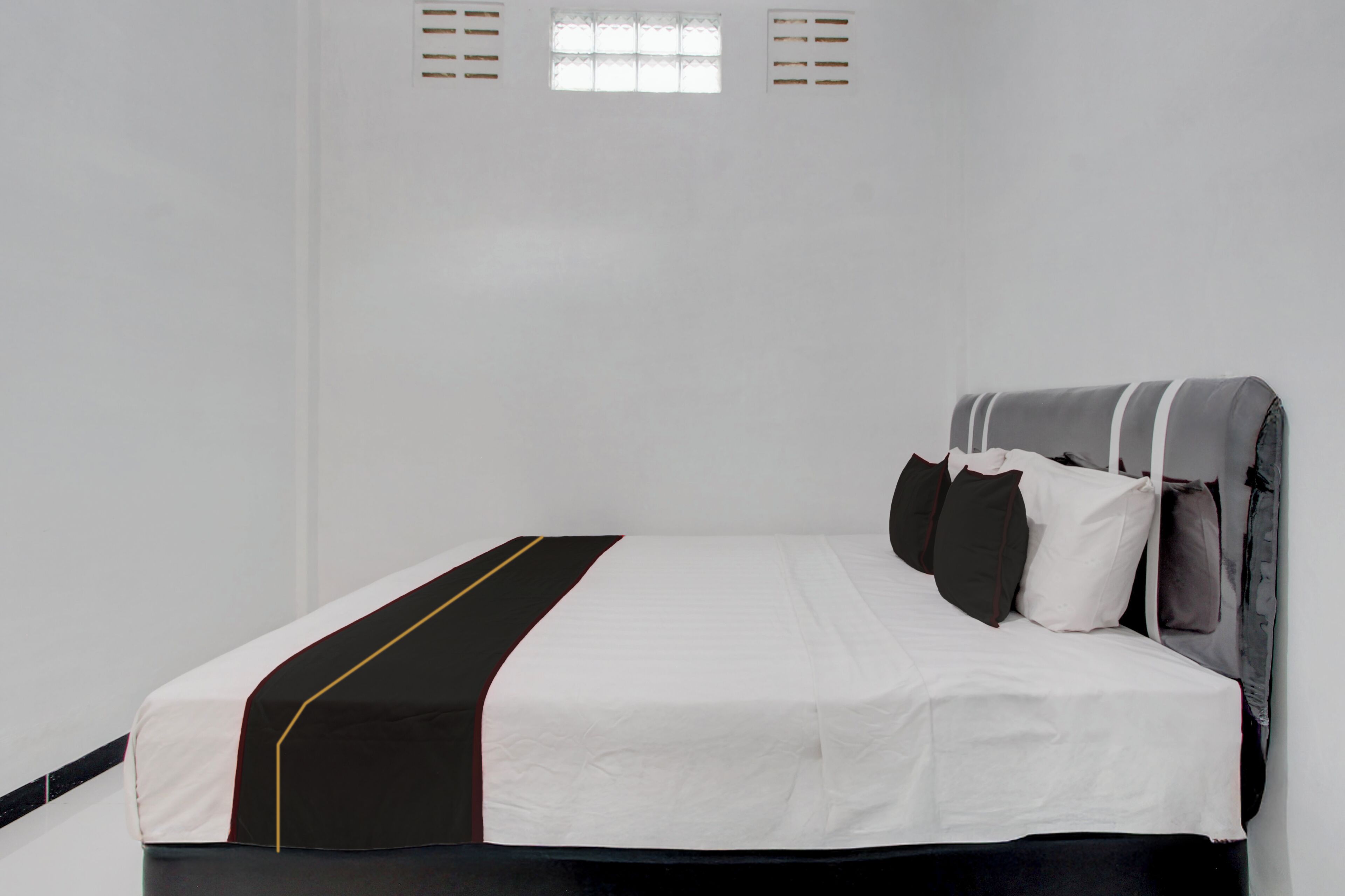 Uma cama com colchão branco, almofadas de destaque preto e vermelho, e cabeceira cinza.