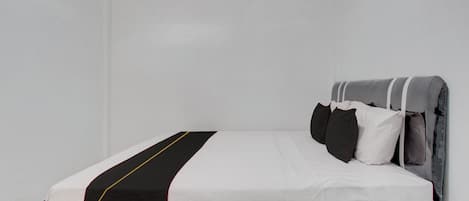 Uma cama com colchão branco, almofadas de destaque preto e vermelho, e cabeceira cinza.
