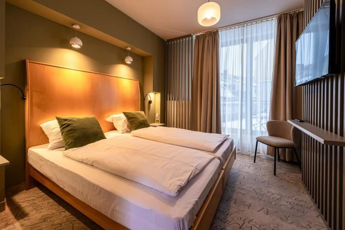 Quarto de hotel com uma cama grande, uma escrivaninha, uma cadeira e uma televisão.