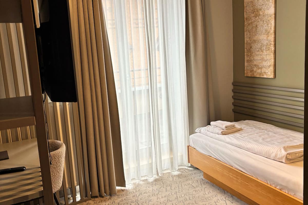 Quarto com cama, luminária pendente, obra de arte na parede e cortinas translúcidas.