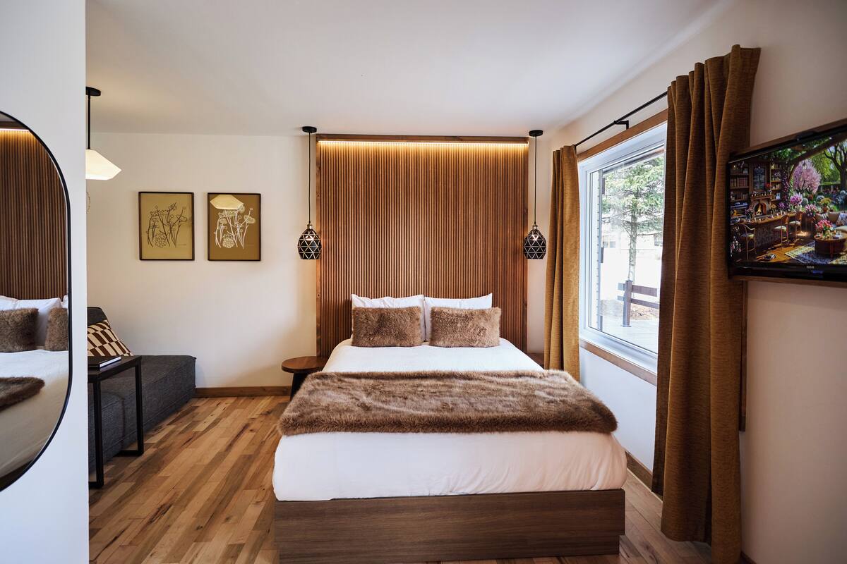 Quarto com cama, sofá, televisão e janela com cortinas.