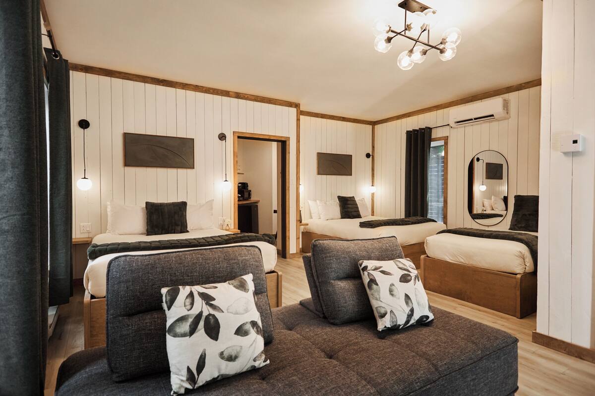 Quarto de hotel com duas camas, um sofá, um espelho e um lustre.