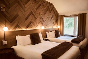 Quarto de hotel com duas camas, painéis de madeira na parede e uma janela com cortinas.