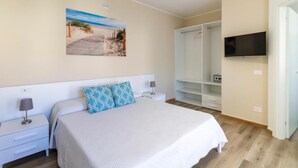Quarto com cama, mesas de cabeceira, televisão, guarda-roupa e arte de parede com tema praiano.