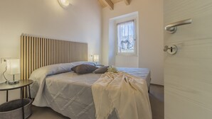 Quarto com cama, mesas de cabeceira, abajur, janela e porta.