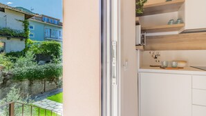 Cozinha com armários brancos, bancada de madeira e vista para a rua com edifícios e vegetação.