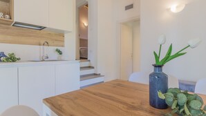 Uma cozinha moderna com armários brancos, bancada de madeira e um vaso com folhas verdes e flores brancas.