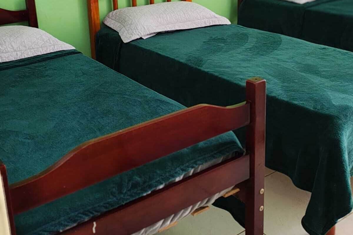 Duas camas de solteiro com estruturas de madeira e roupa de cama verde em um quarto com paredes e piso de azulejos verdes.