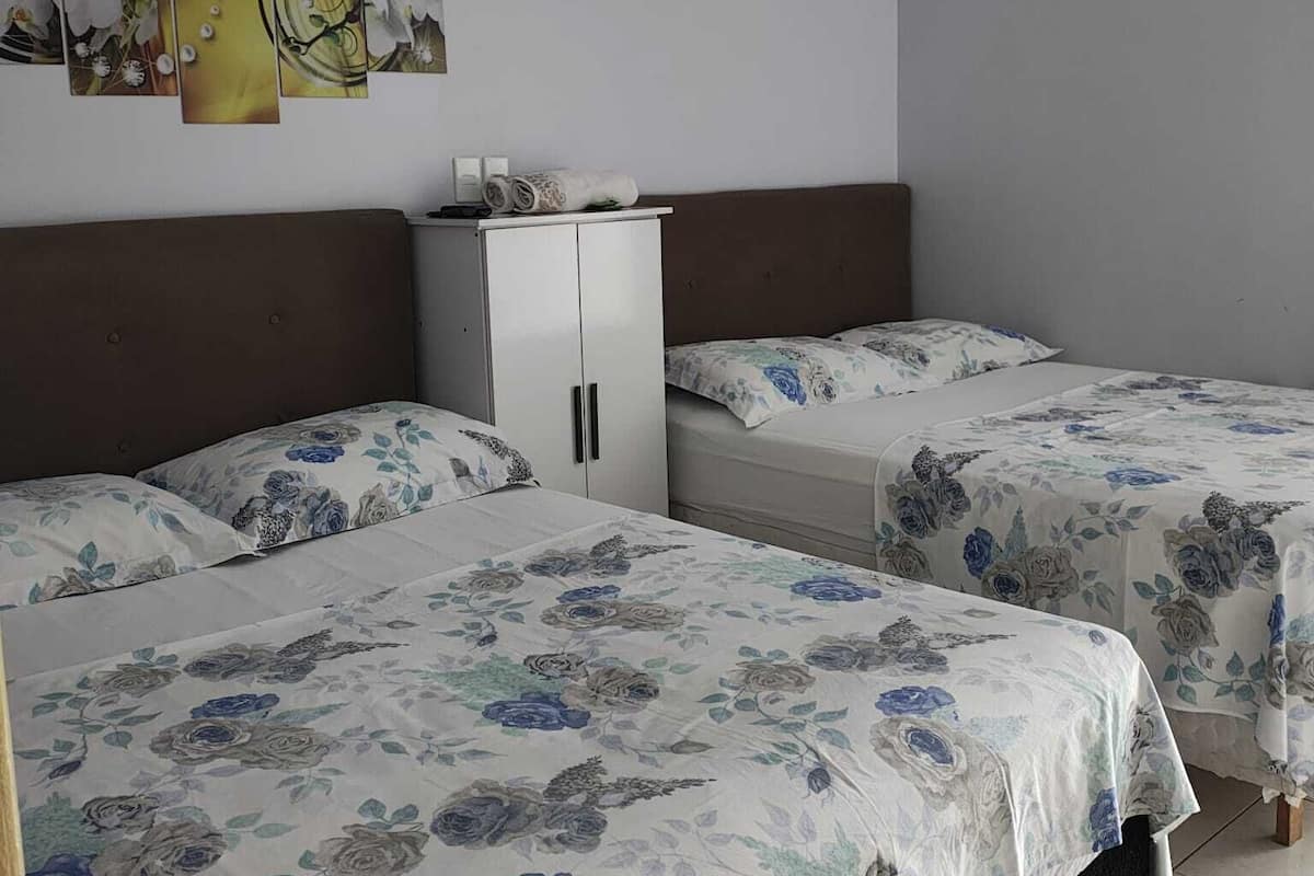 Quarto com duas camas, um guarda-roupa branco e uma parede com arte floral.