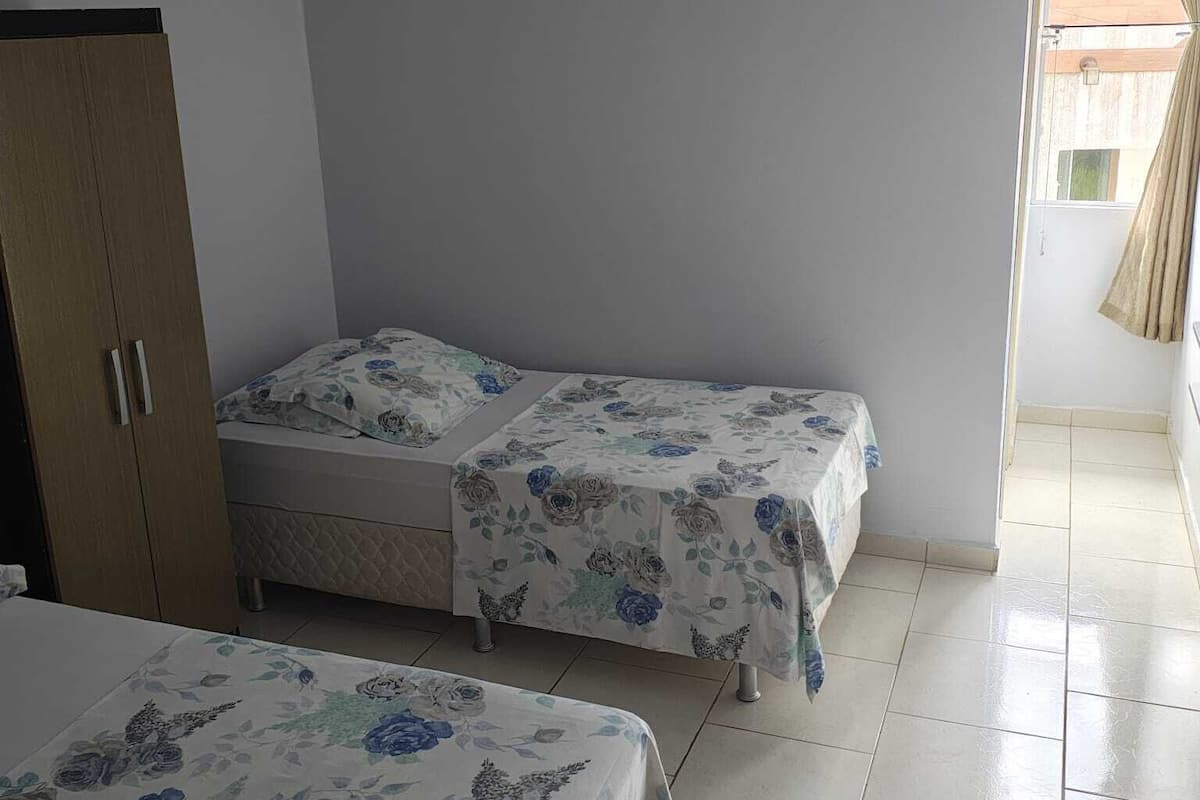 Quarto com duas camas, um guarda-roupa e uma janela com cortinas.