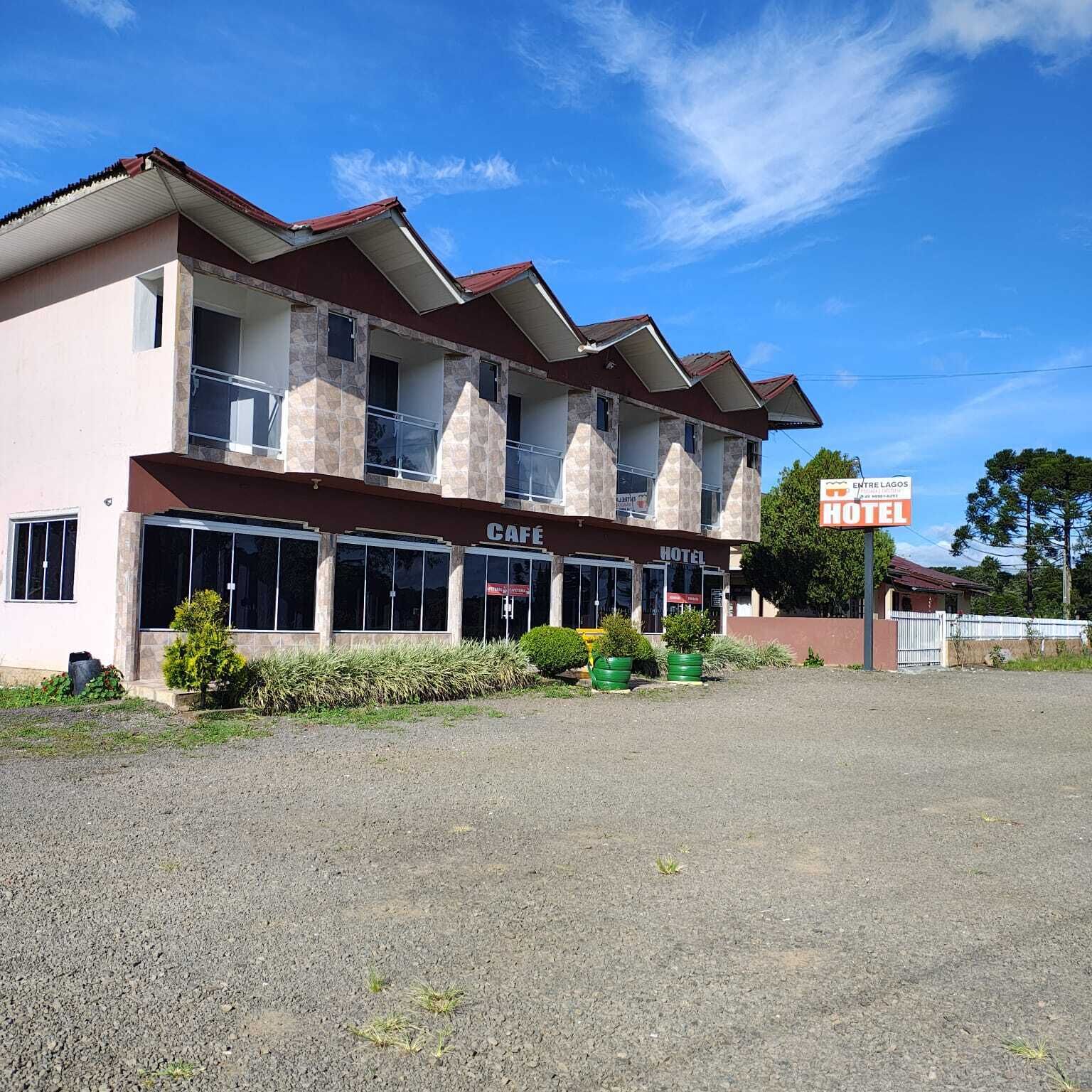 Um edifício de dois andares com café e placa de hotel, com telhado plano e entrada por um caminho de cascalho.