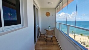 Uma varanda com vista para o oceano, uma mesa pequena com cadeiras e um painel decorativo na parede.