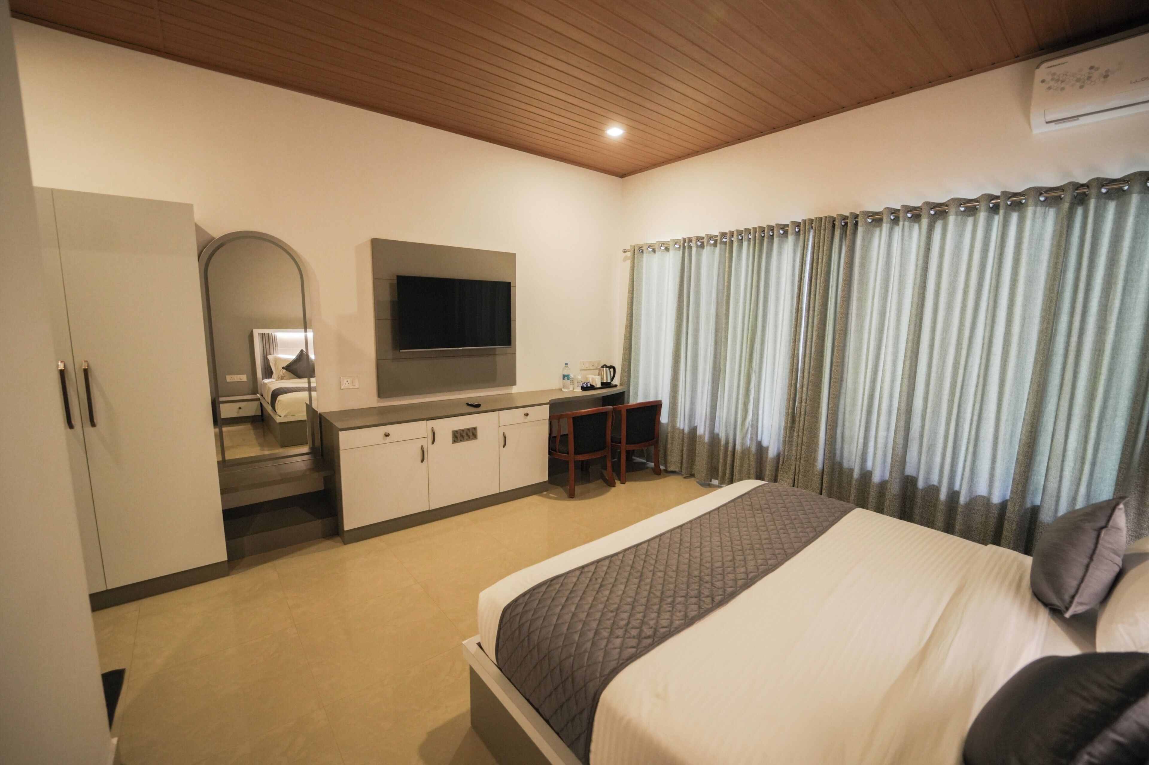 Quarto de hotel com cama, secretária com cadeira, televisão e guarda-roupa.