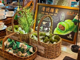 Exposição de comidas típicas, incluindo bolinhos verdes e um letreiro com caracteres chineses.