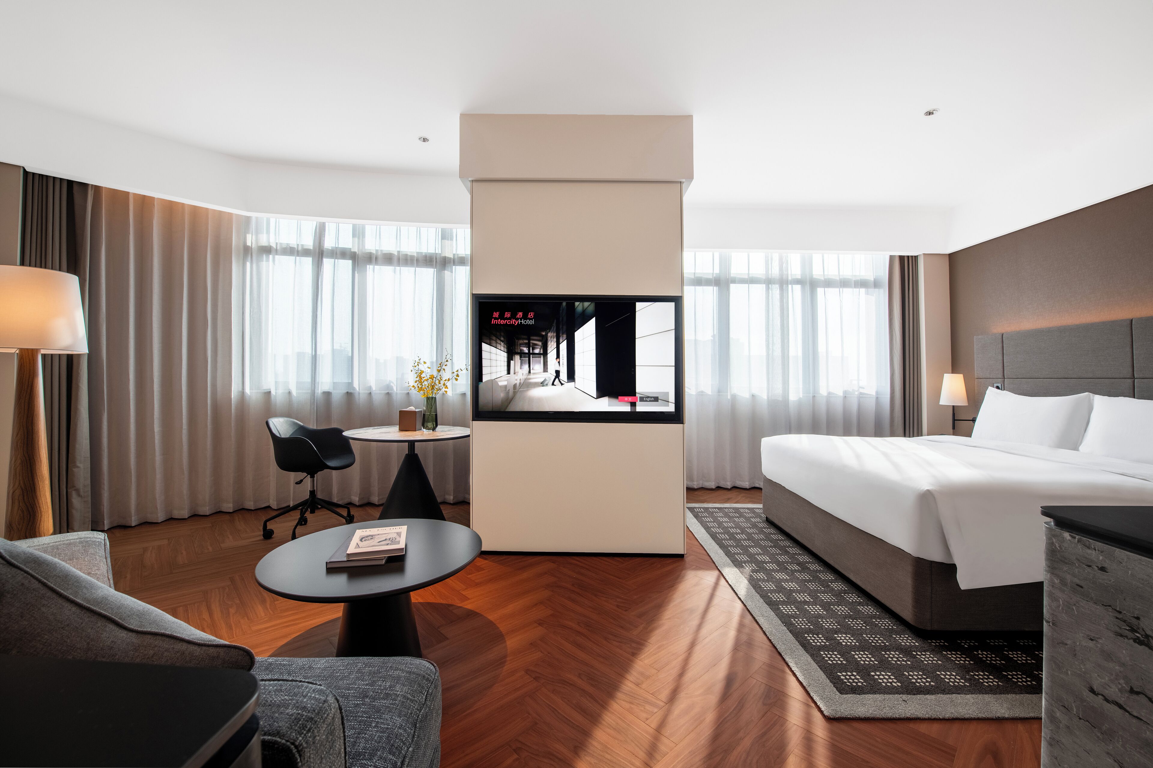 Quarto de hotel moderno com cama, escrivaninha, cadeira e televisão.