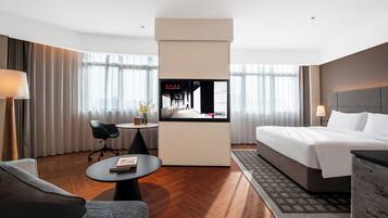 Quarto de hotel moderno com cama, escrivaninha, cadeira e televisão.