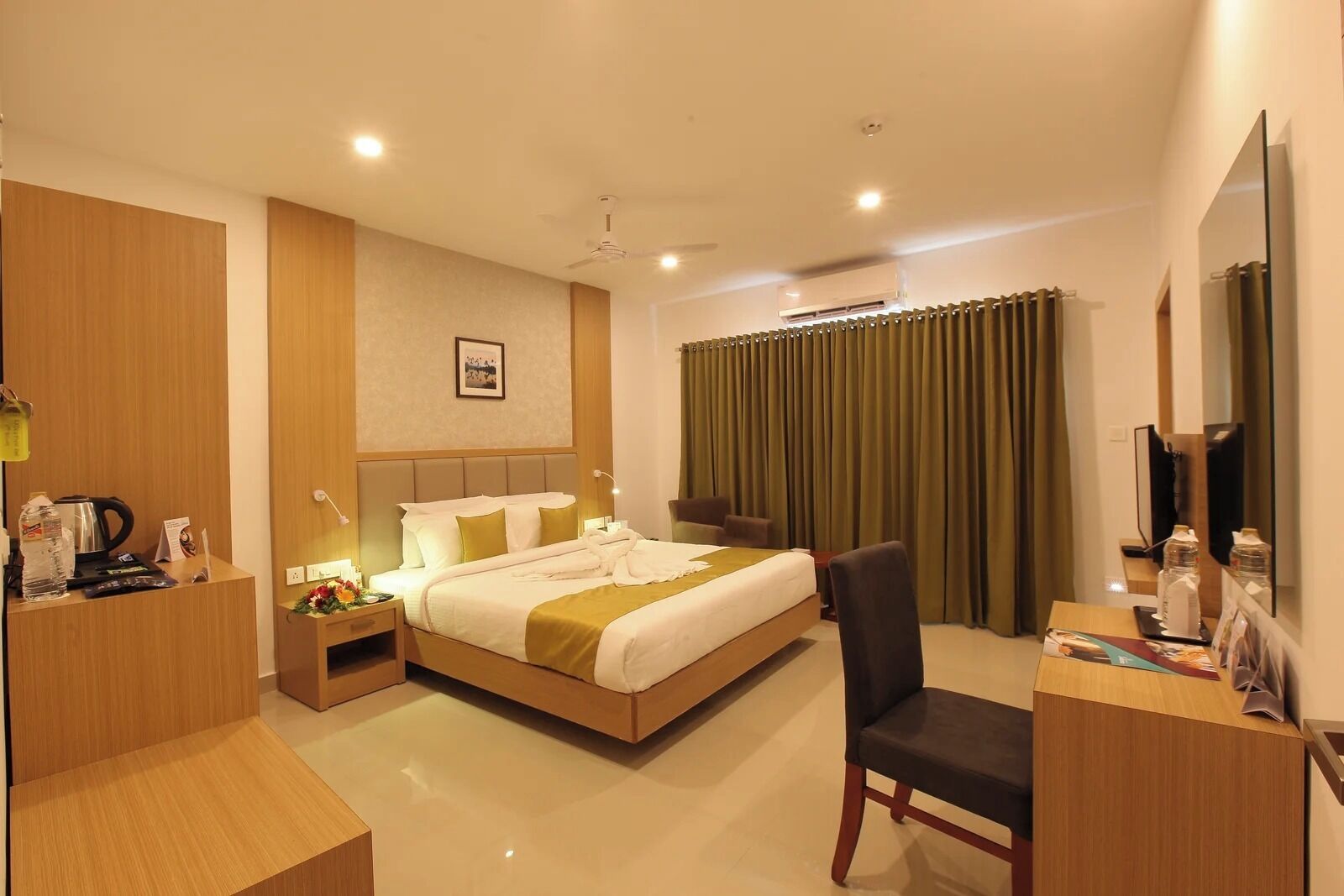 Quarto de hotel com cama, escrivaninha, cadeira, mesa de cabeceira e cortinas.