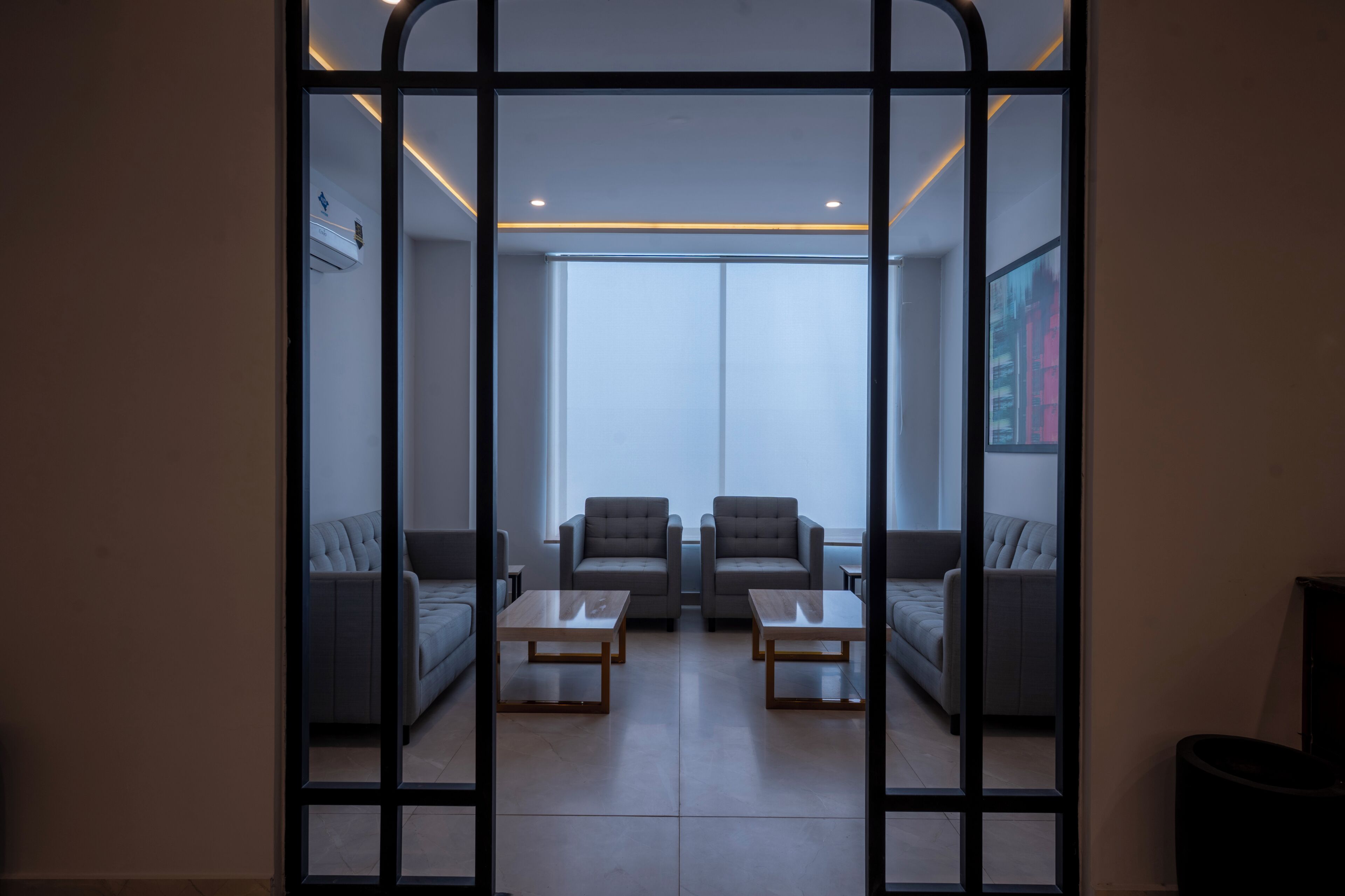 Uma sala de estar moderna com dois sofás, duas poltronas e duas mesas de centro, separadas por um painel de vidro.