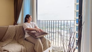 Uma pessoa sentada em um sofá com vista para um horizonte urbano através de uma varanda.