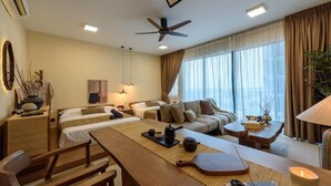 Quarto de hotel com cama, sofá, mesa de jantar, cadeiras, ventoinha no teto e uma janela grande com cortinas.