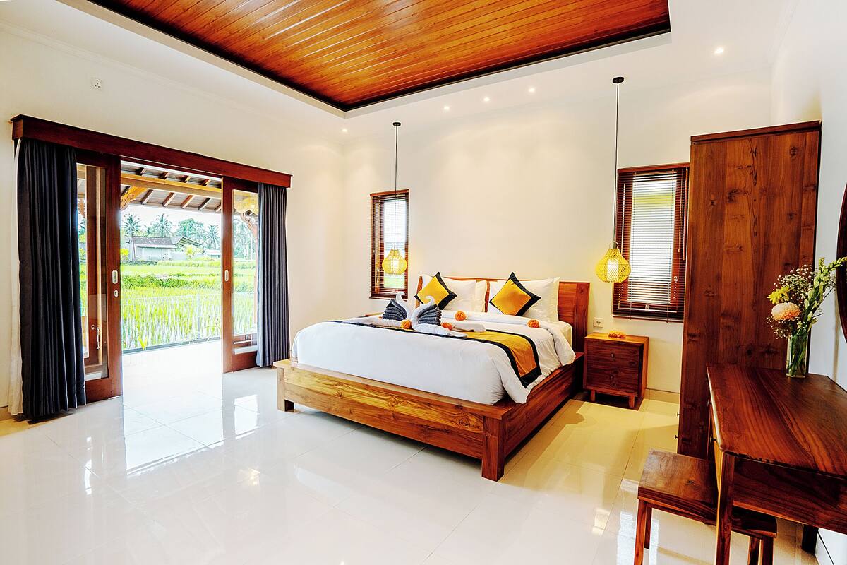 Quarto com uma cama grande, móveis de madeira e vista para uma paisagem verde.