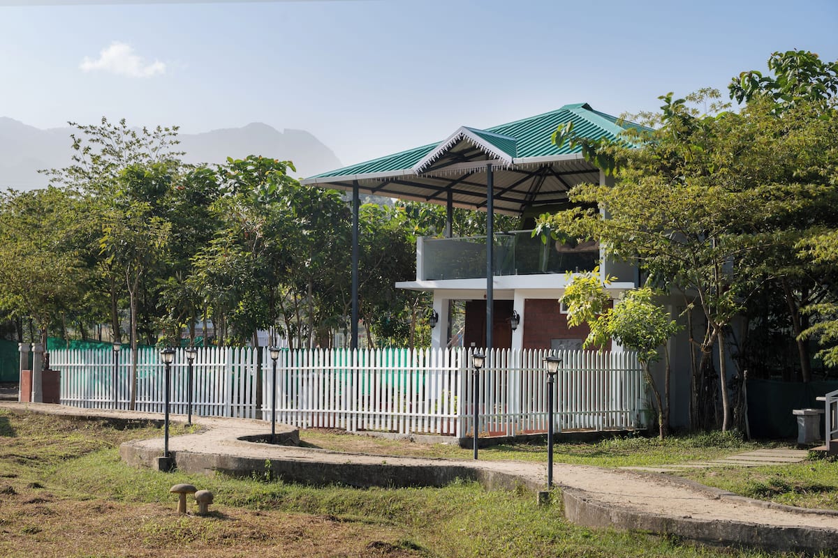 Um edifício com telhado verde, cercado por uma cerca branca, árvores e céu claro.