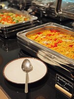 Buffet com diversos pratos, uma colher em um prato e uma placa com texto.