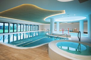 Piscina interior com hidromassagem, amplas janelas e design moderno no teto.