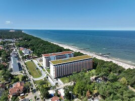 Vista aérea de uma área costeira com um edifício moderno, uma praia e uma estrada.