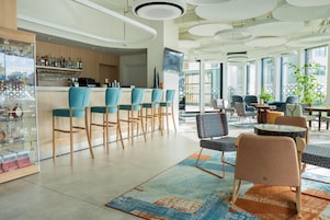 Uma área de bar moderna, com banquetas, balcão com vitrine de vidro e um espaço de estar com diversas cadeiras e mesas.