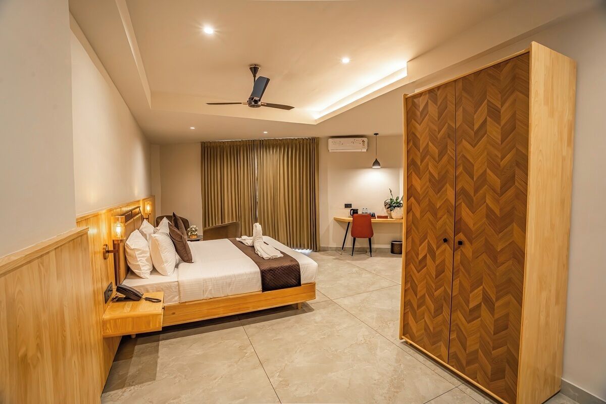 Quarto de hotel com cama, escrivaninha, armário e ventoinha no teto.
