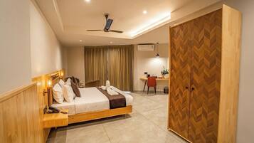 Quarto de hotel com cama, escrivaninha, armário e ventoinha no teto.