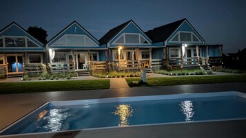 Uma casa moderna com piscina, janelas amplas e varanda frontal bem iluminada.