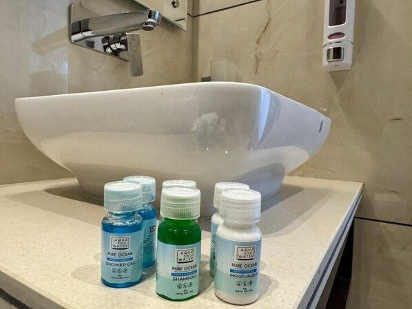 Casa de banho com uma bacia branca grande, três frascos de produtos Aqua Shui Water e uma torneira moderna.