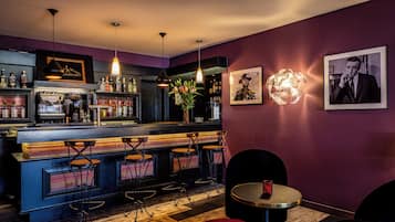 Uma área de bar com banquetas, balcão e uma mesa redonda com almofada vermelha.