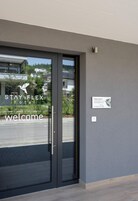 Entrada moderna de hotel com porta de vidro, placa de boas-vindas e sinalização indicando a entrada.