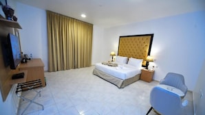 Quarto de hotel com cama, duas luminárias de cabeceira, escrivaninha com cadeira, televisão e janela com cortinas.