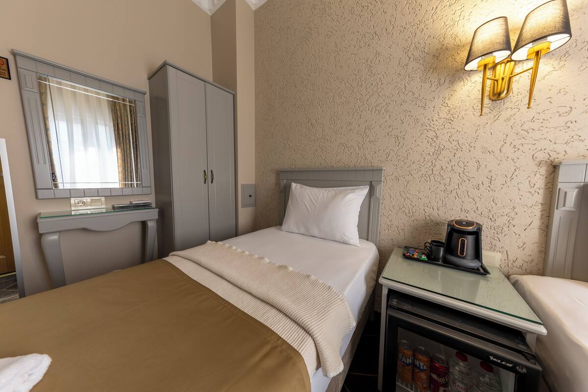 Quarto de hotel com cama, mesa de cabeceira, cafeteira, minibar, espelho e guarda-roupa.