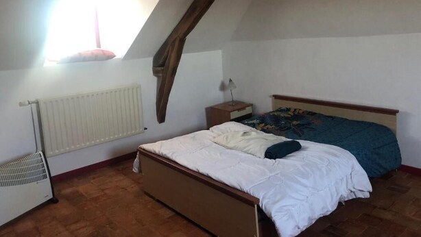 Quarto com teto inclinado, cama, mesa de cabeceira, radiador e janela.