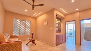 Uma sala de estar espaçosa com sofá, mesa de centro de vidro, ventilador de teto e vista para uma varanda.