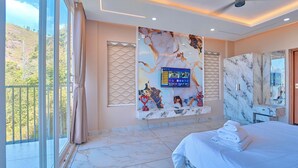 Quarto com uma cama grande, televisão na parede e varanda com vista para as colinas.
