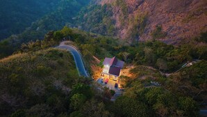 Uma casa com uma entrada em curva, rodeada por uma floresta densa e colinas.
