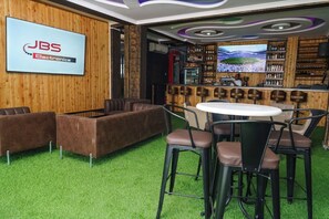 Uma área de bar com uma tela de televisão, banquetas e um sofá.