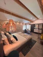 Quarto com cama grande, parede de pedra, teto de madeira e banheiro com espelho e pia.